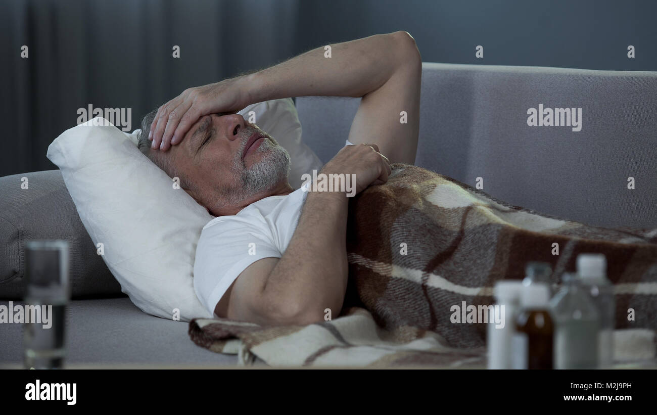 Ill senior male lying in bed and suffering from terrible headache ...