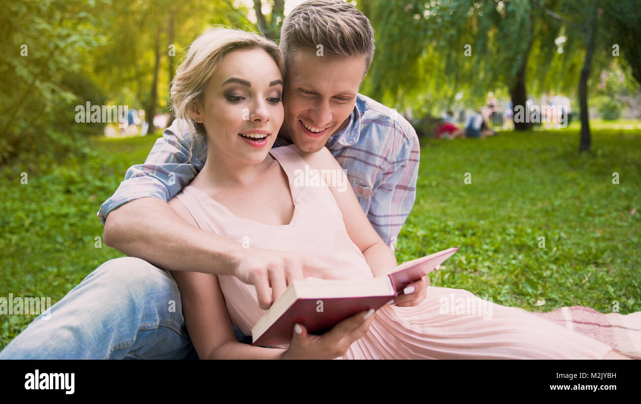 Couple of students in love sitting on rug reading educational book ...