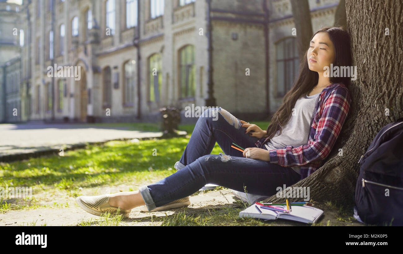 Mixed female relaxing under tree with eyes shut, stressful day ...