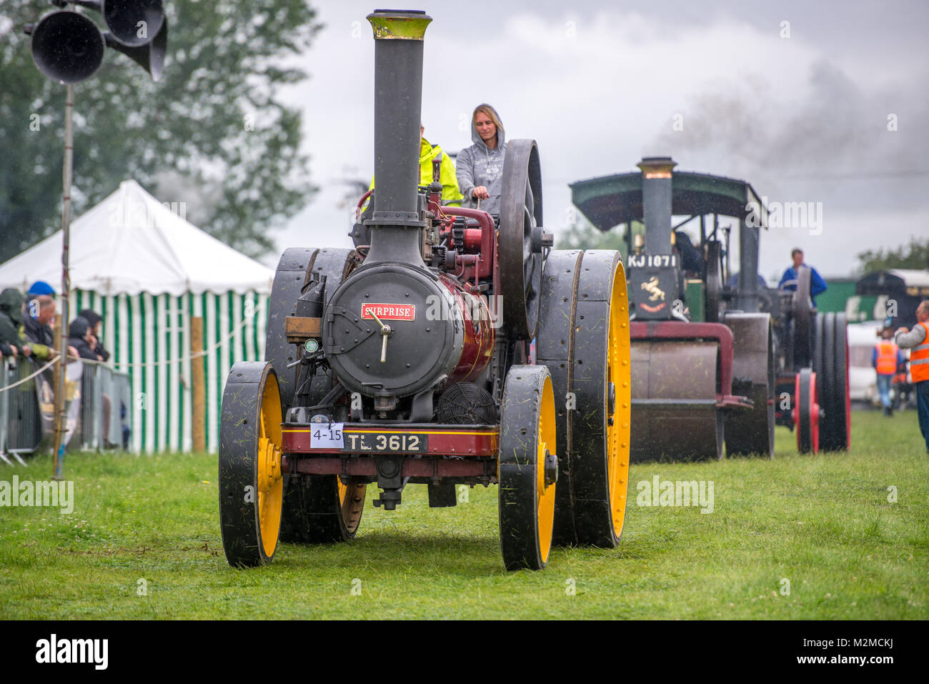 Young female helps operates vintage steam engine tractor as it rides ...