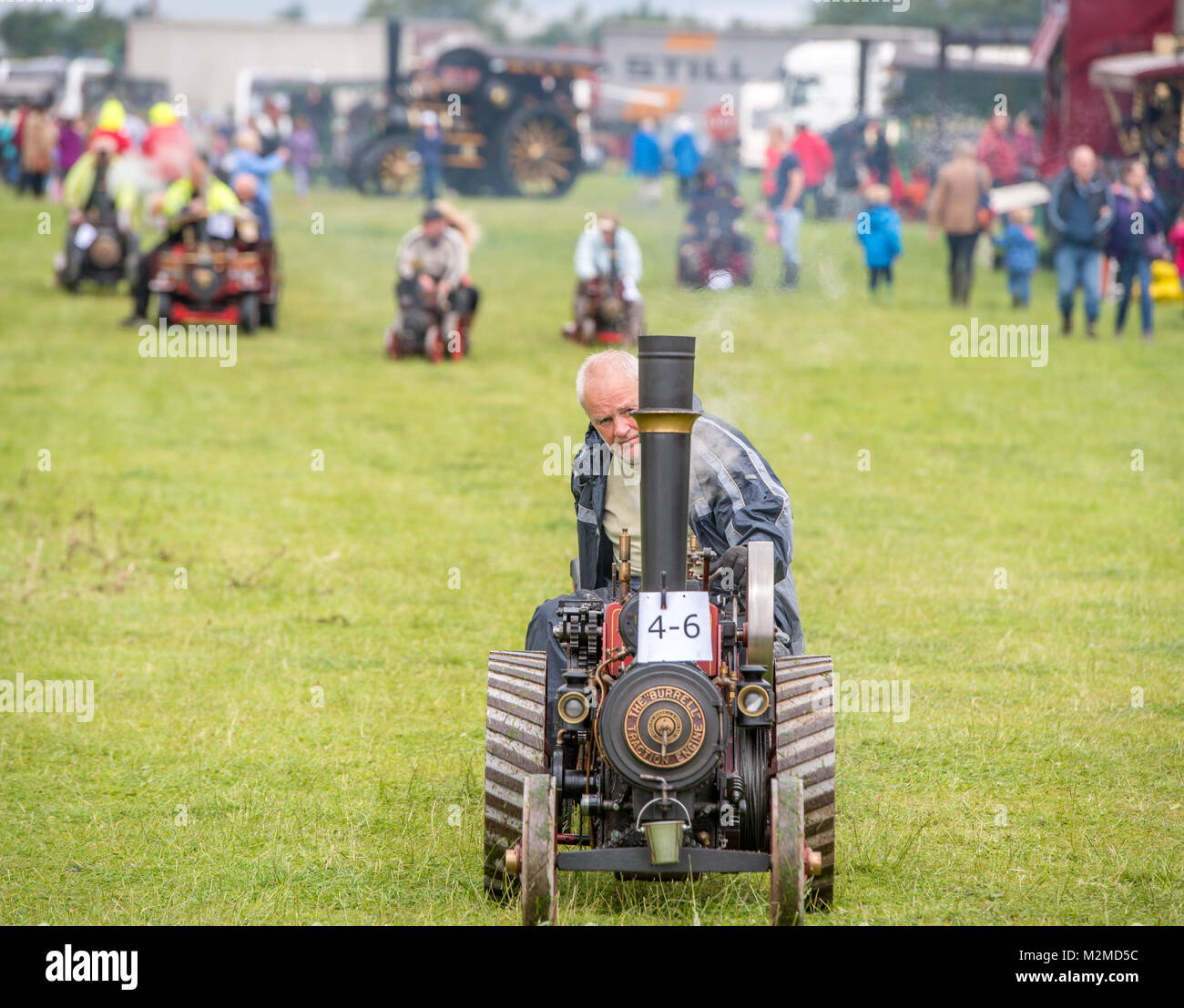 Mature male drives miniature tractor steam engine with others following ...
