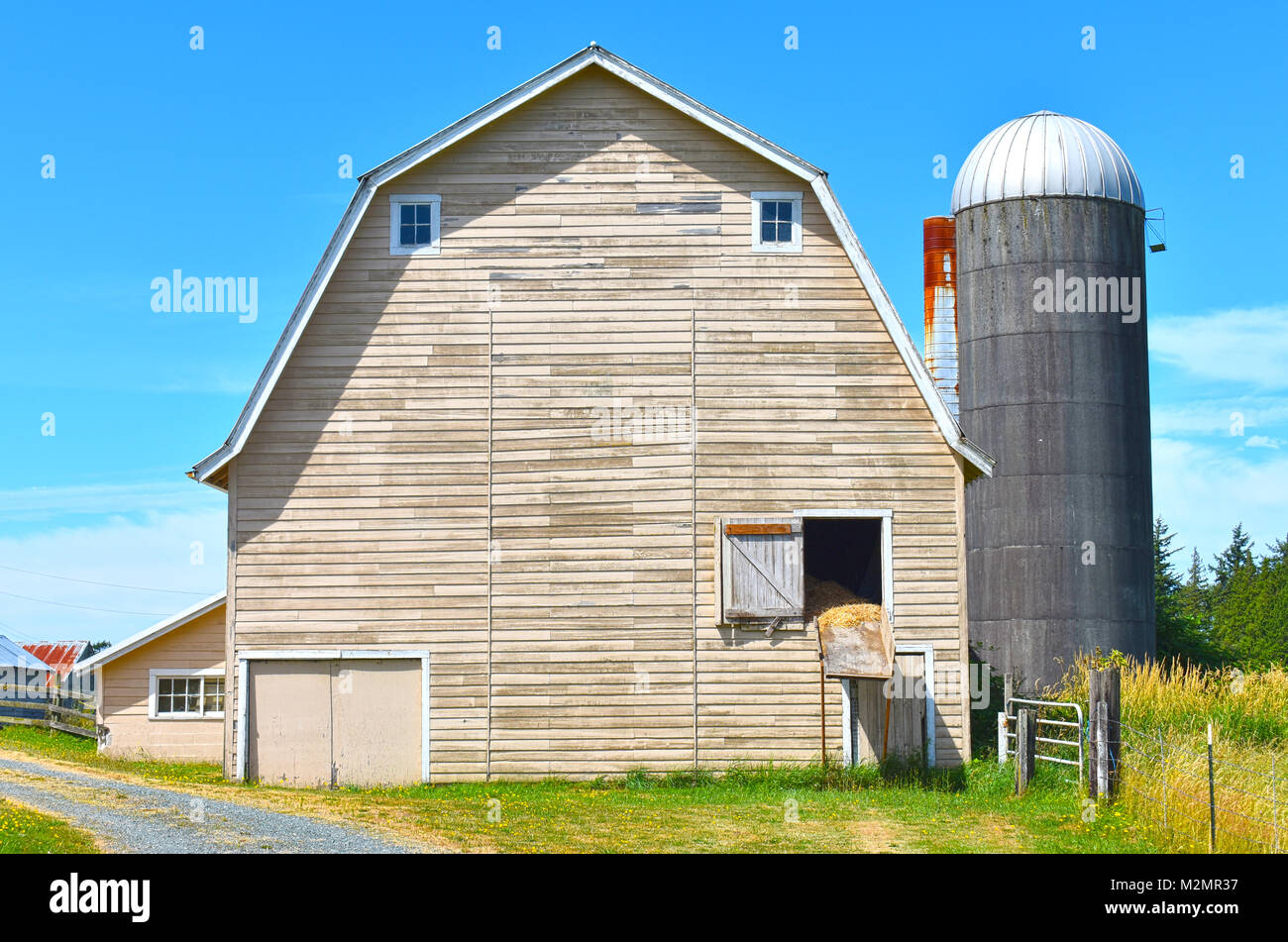 A beautiful country barn with a silo and hay shoot with cloudy blue ...