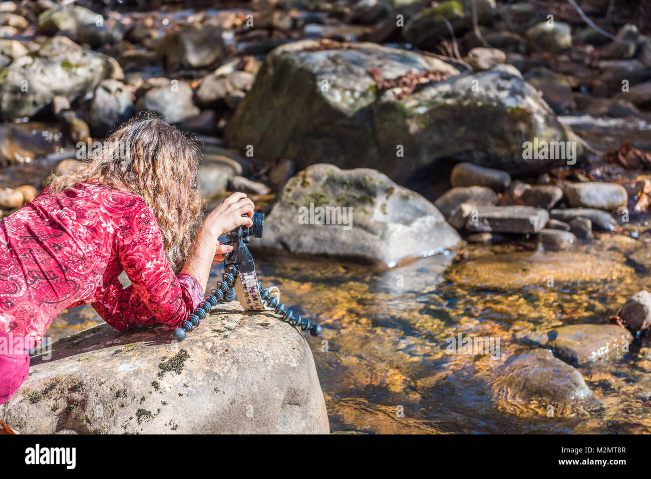 Woman side profile in red lying down taking pictures of shallow rock ...