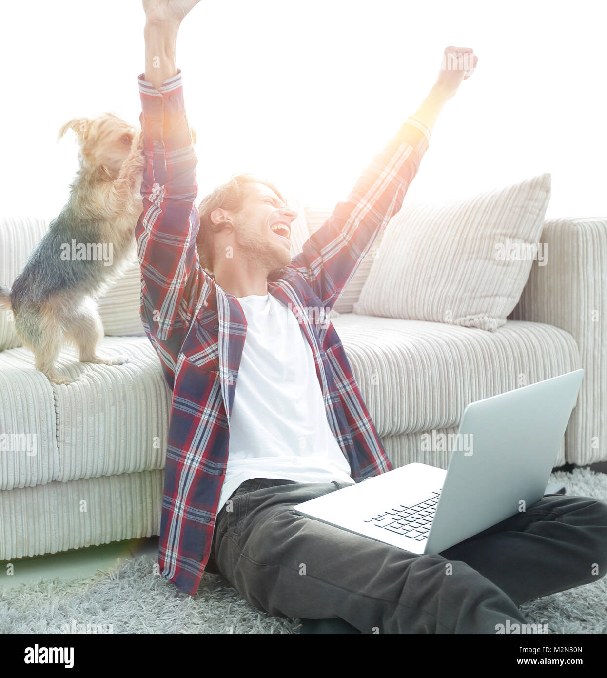 happy guy rejoicing and raising his hands sitting near the sofa in the ...