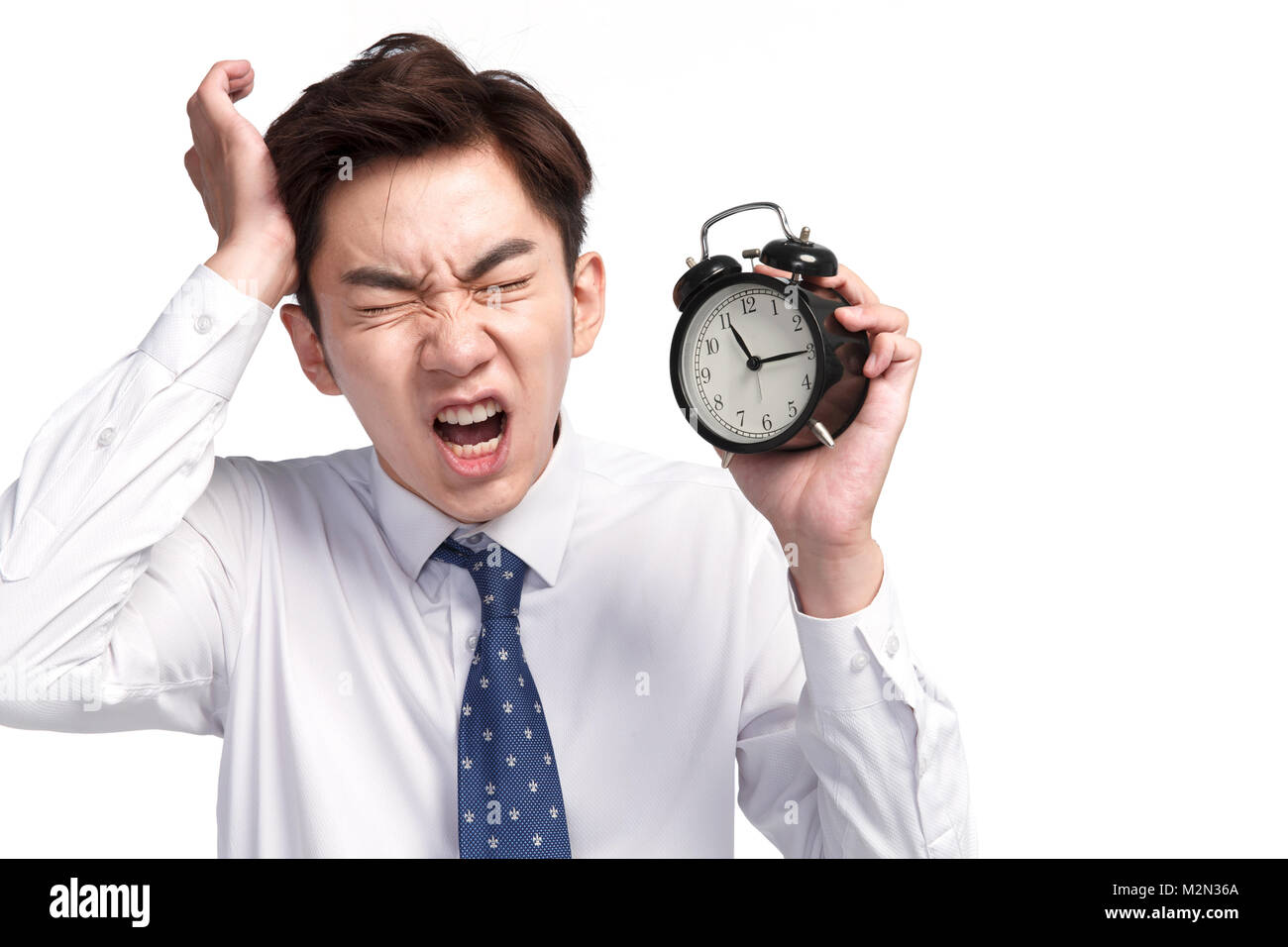 A young business man with an expression of pain holding the alarm clock ...