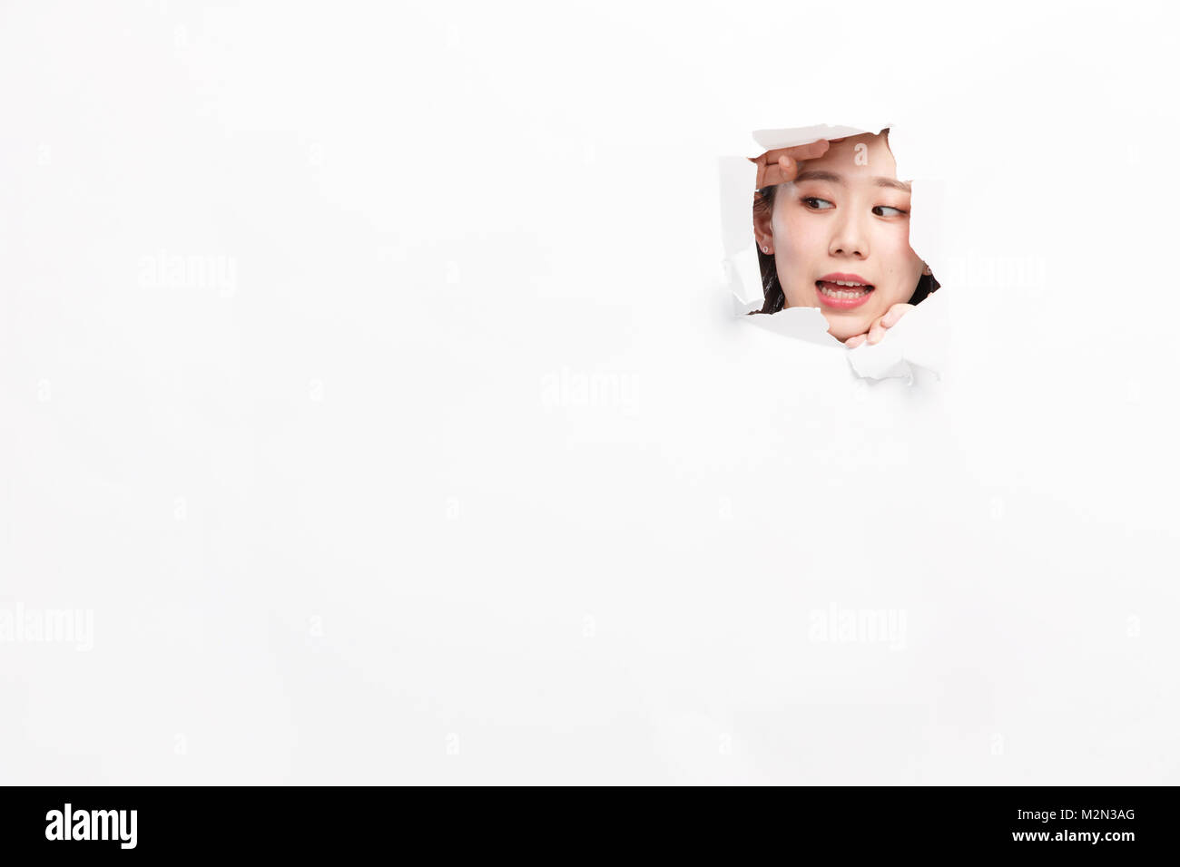 Young woman peeking through paper hole Stock Photo - Alamy