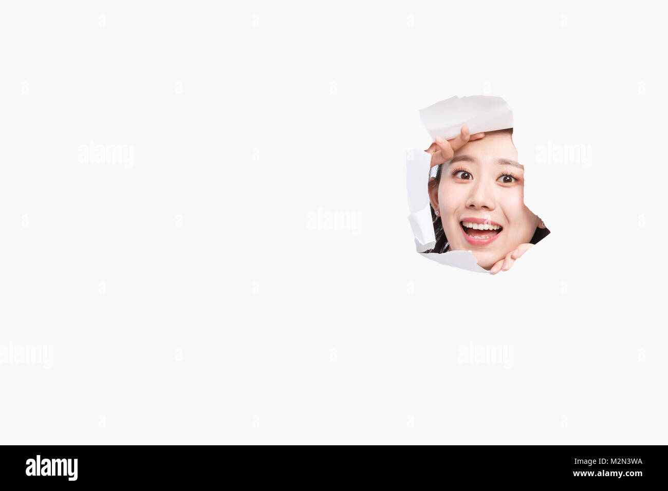 Young woman peeking through paper hole Stock Photo - Alamy