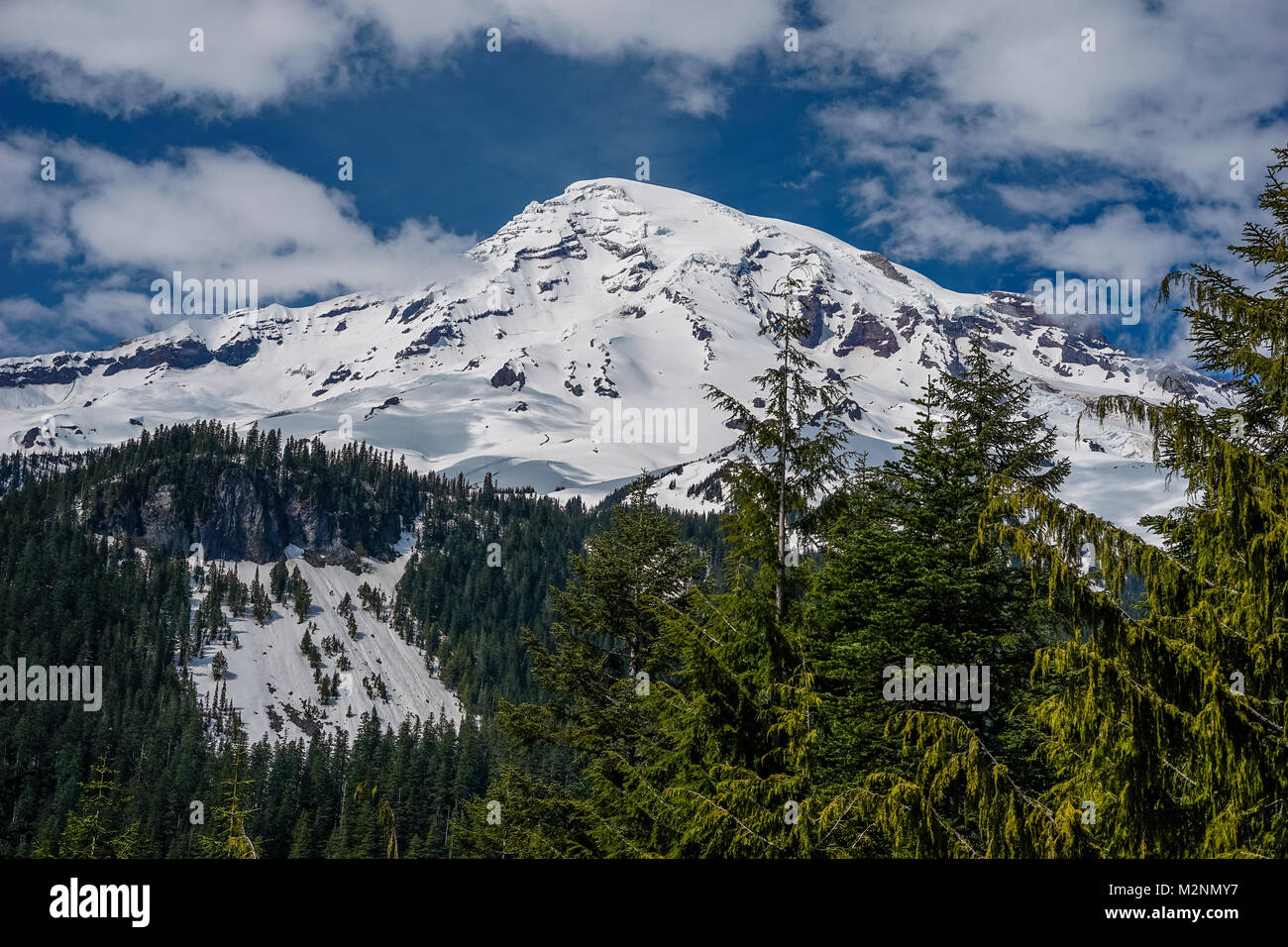 Snowcapped Mountain with evergreen trees blue sky wispy clouds Stock ...