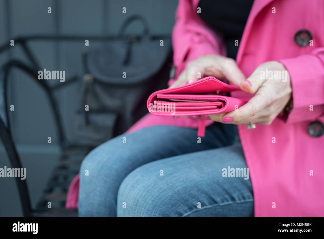 woman sitting on bench wearing coordinating pink coat, wallet and nail ...