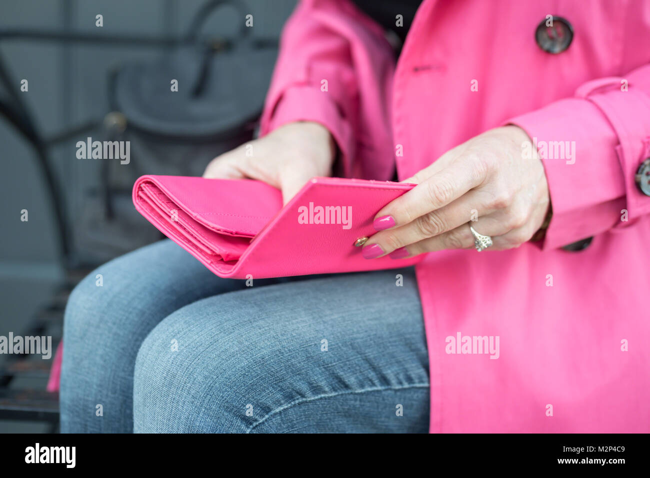 closeup of woman sitting on bench holding pink wallet with pink ...