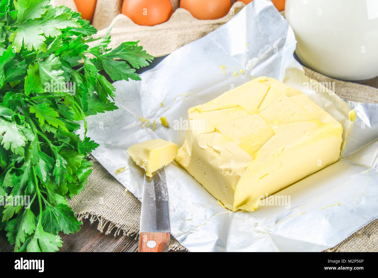 A bar of butter is cut into pieces on a wooden board with a knife ...