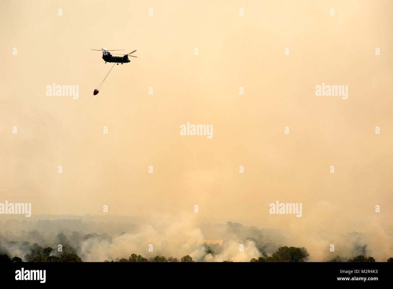 A Texas National Guard CH-47 Chinook flies over the smoke to dump its ...