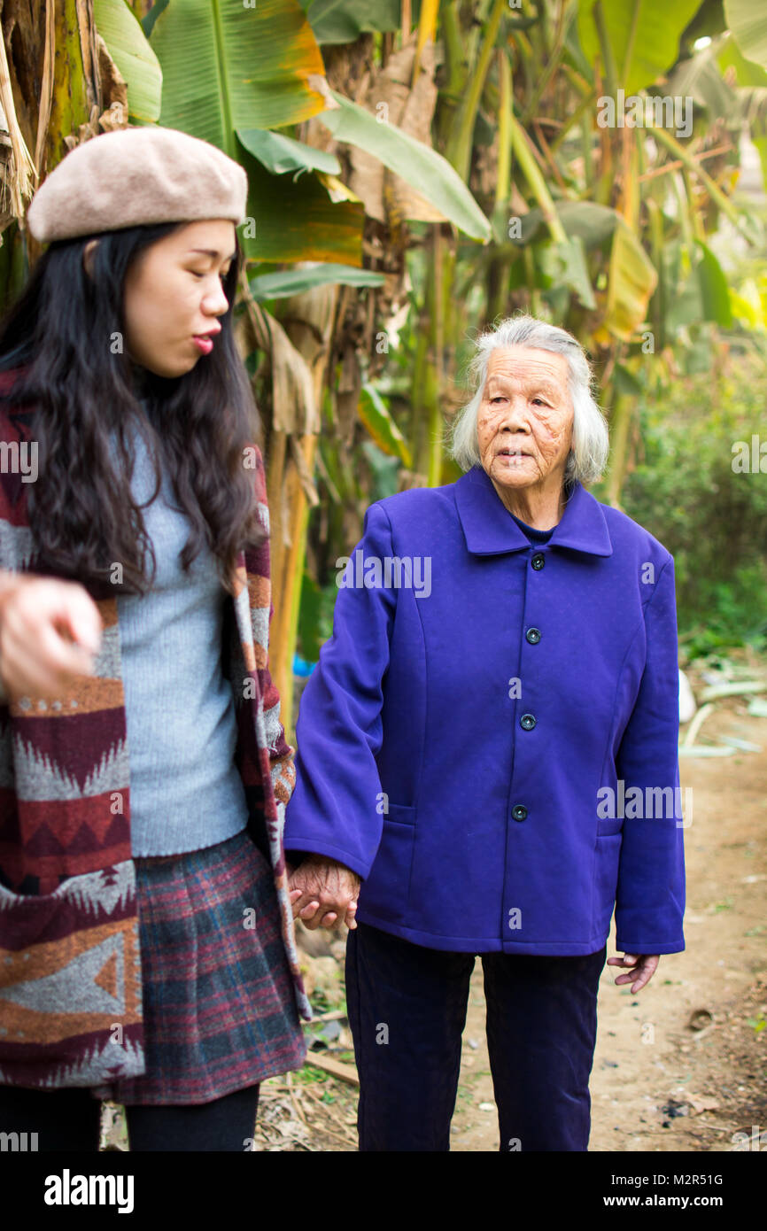 Asian girl having a walk with her grandma in green tropical environment ...