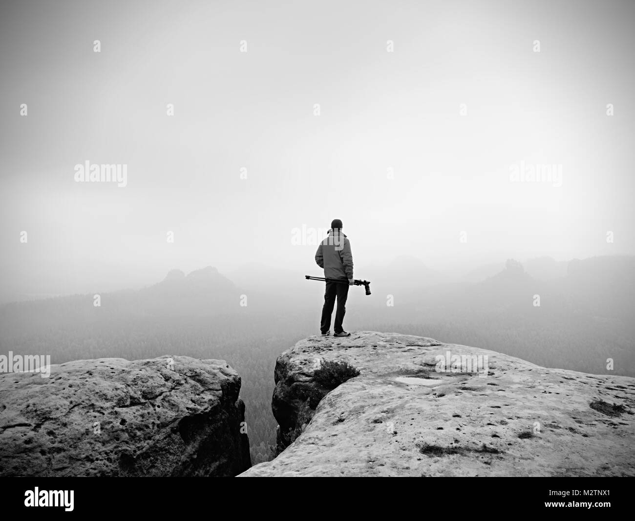Hiker with camera on tripod takes picture from rocky summit. Alone ...