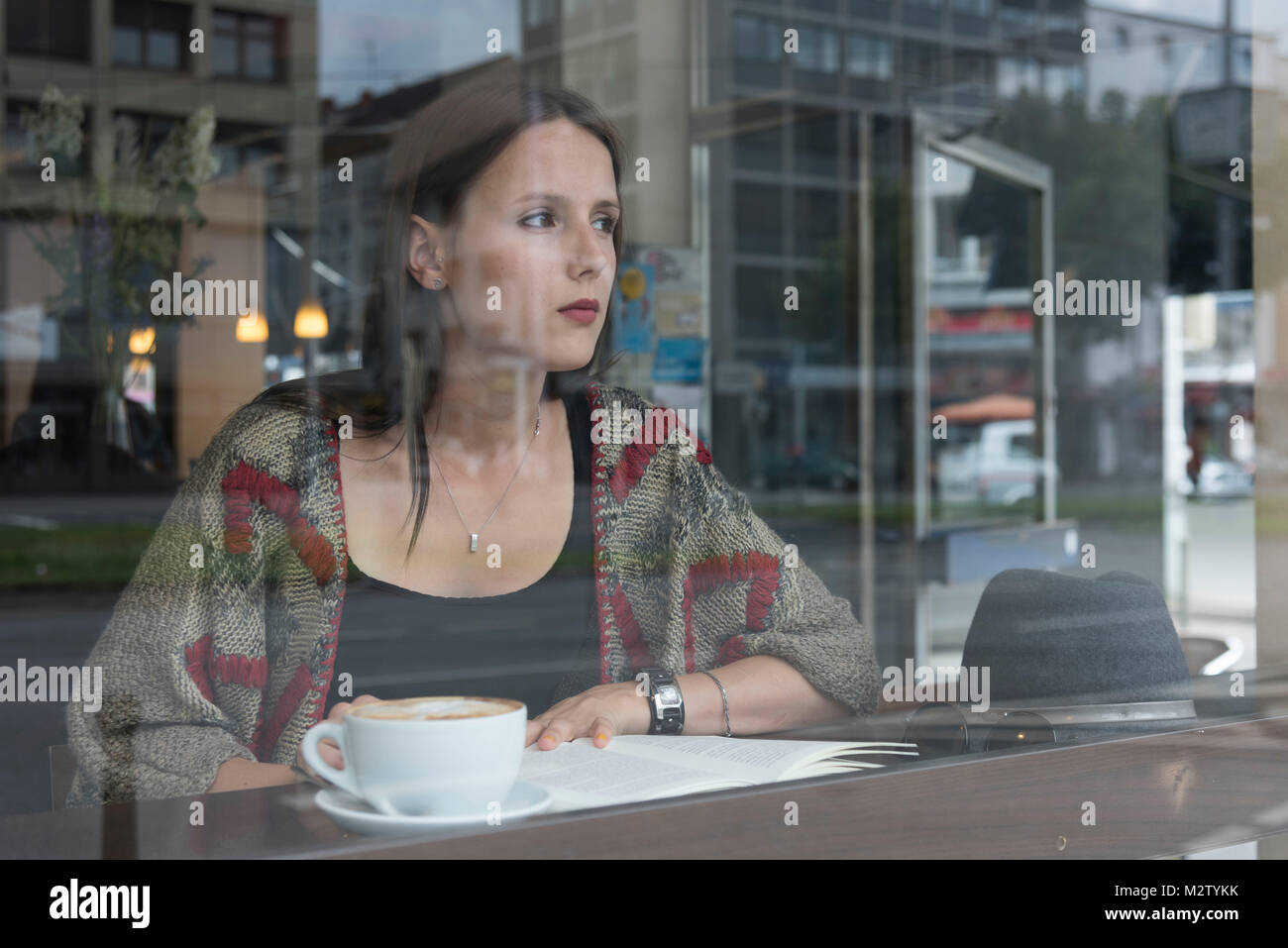 Young woman behind window while reading in the café, thoughtful, semi ...