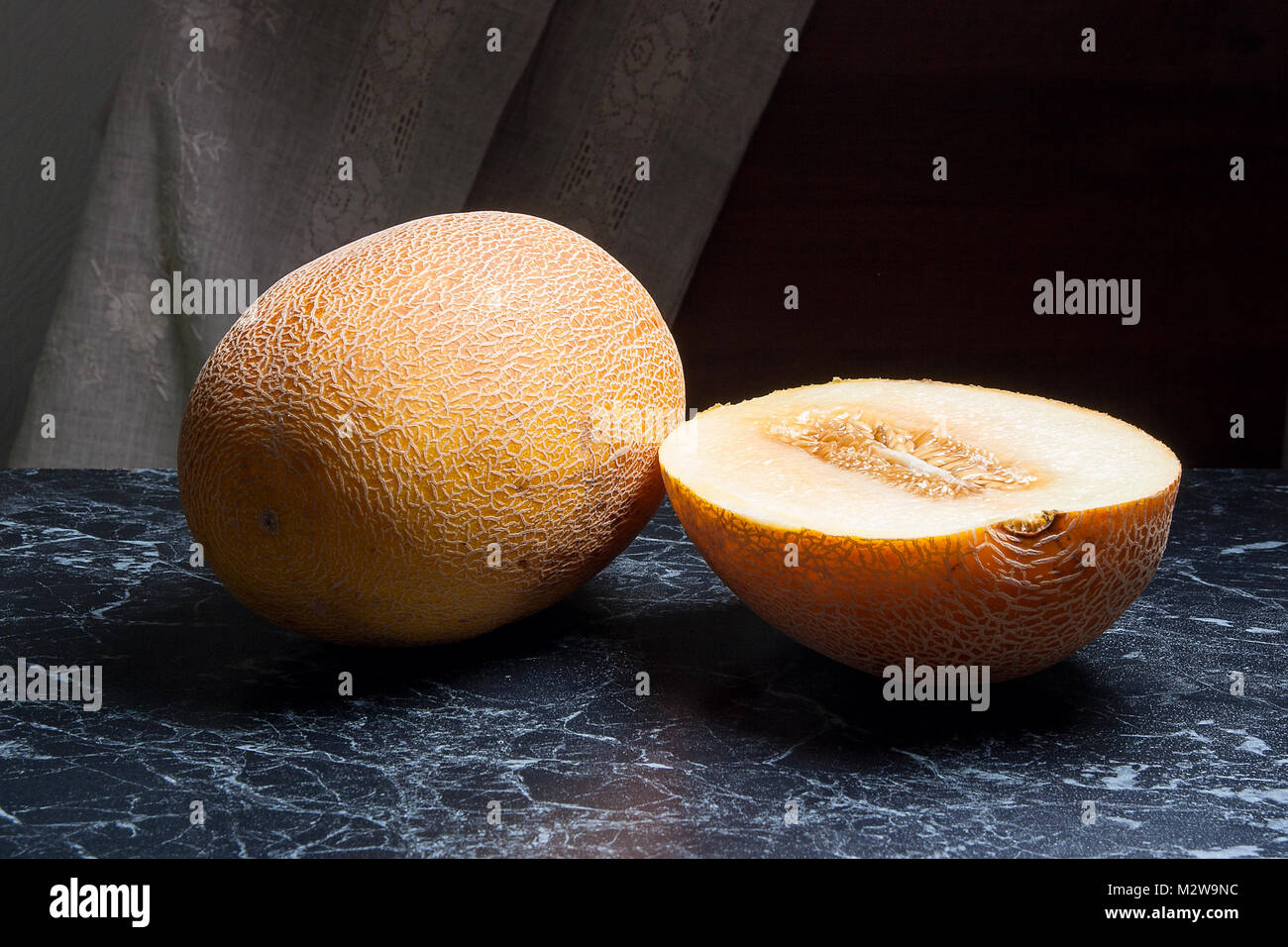 Ripe whole and half honeydew melon fruit at summer time on dark marble ...