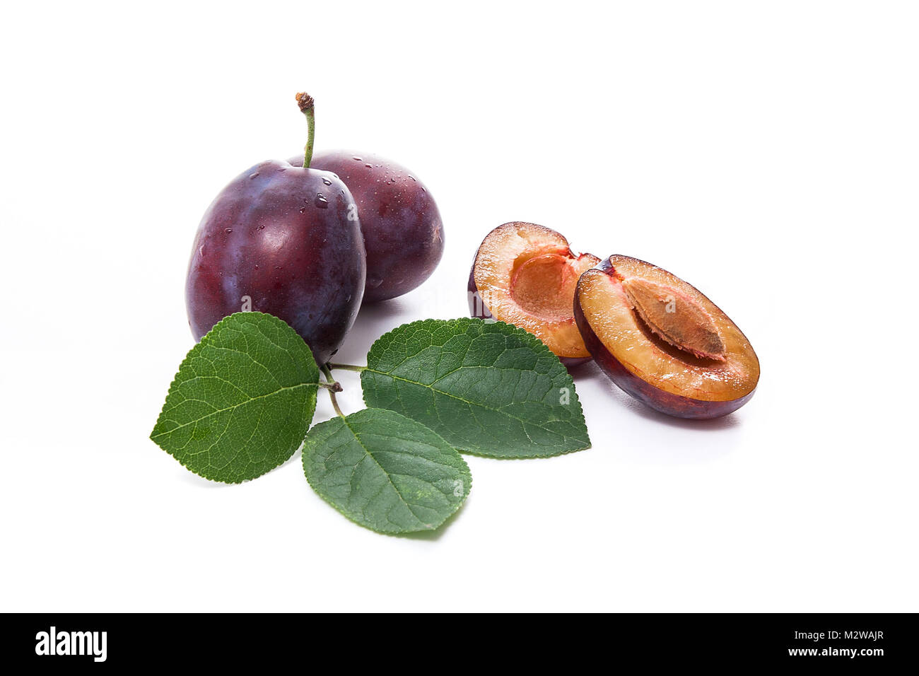 Two whole and half of sweet juicy plums with big green leaf isolated on ...