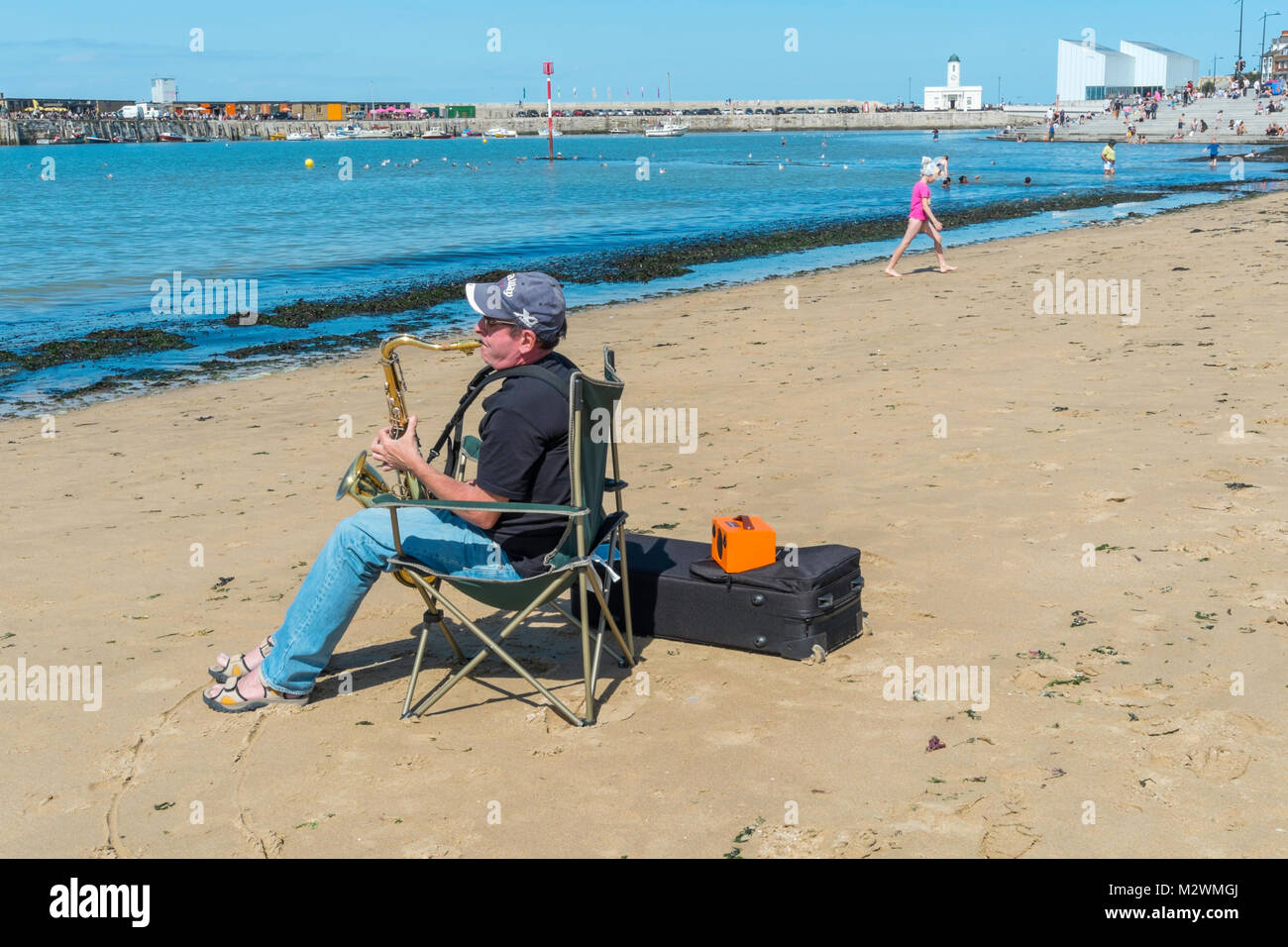 A musician playing a saxophone on Margate beach in the sunshine Stock ...