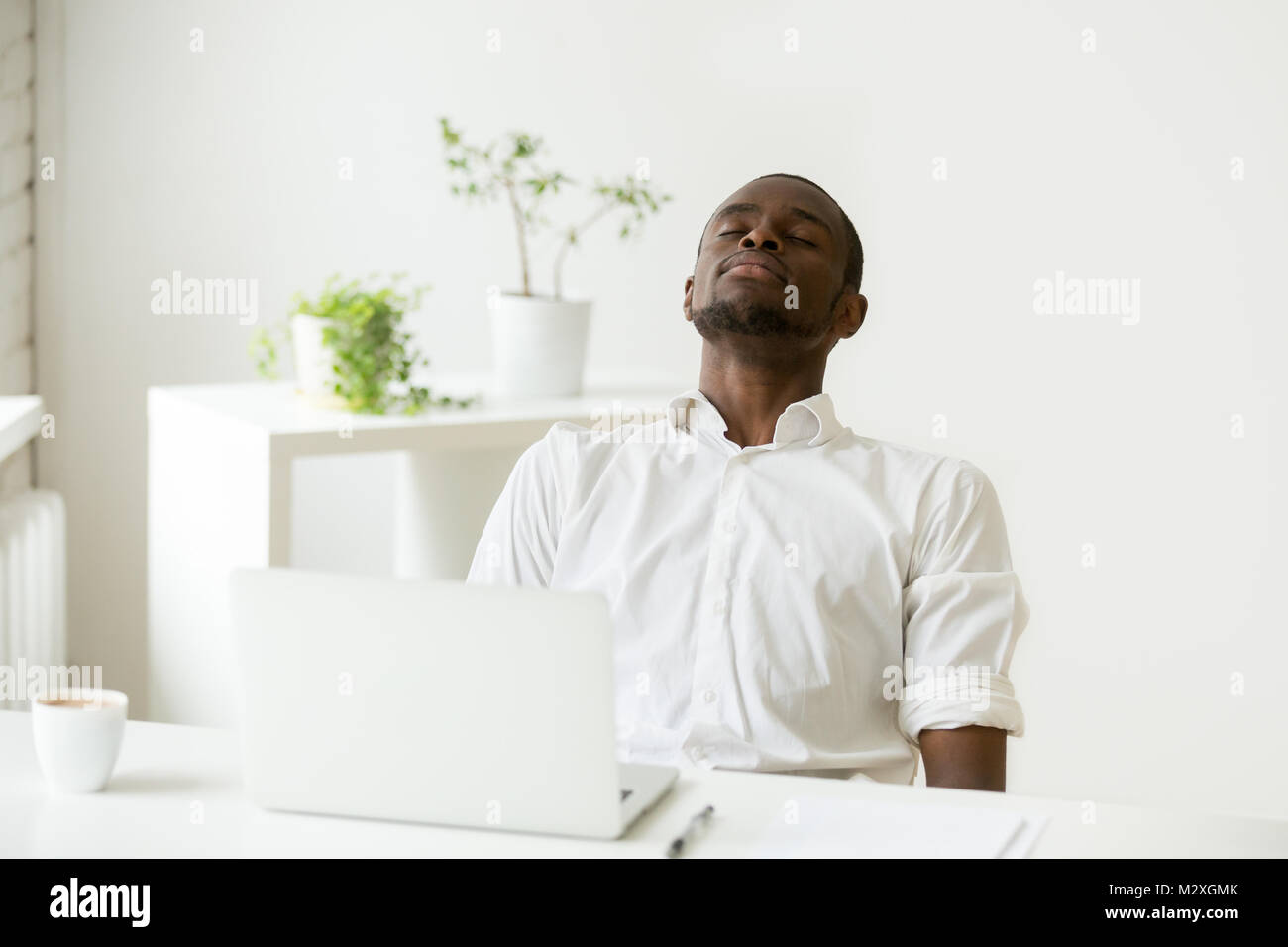 African office worker relaxing with eyes closed sitting at work desk ...