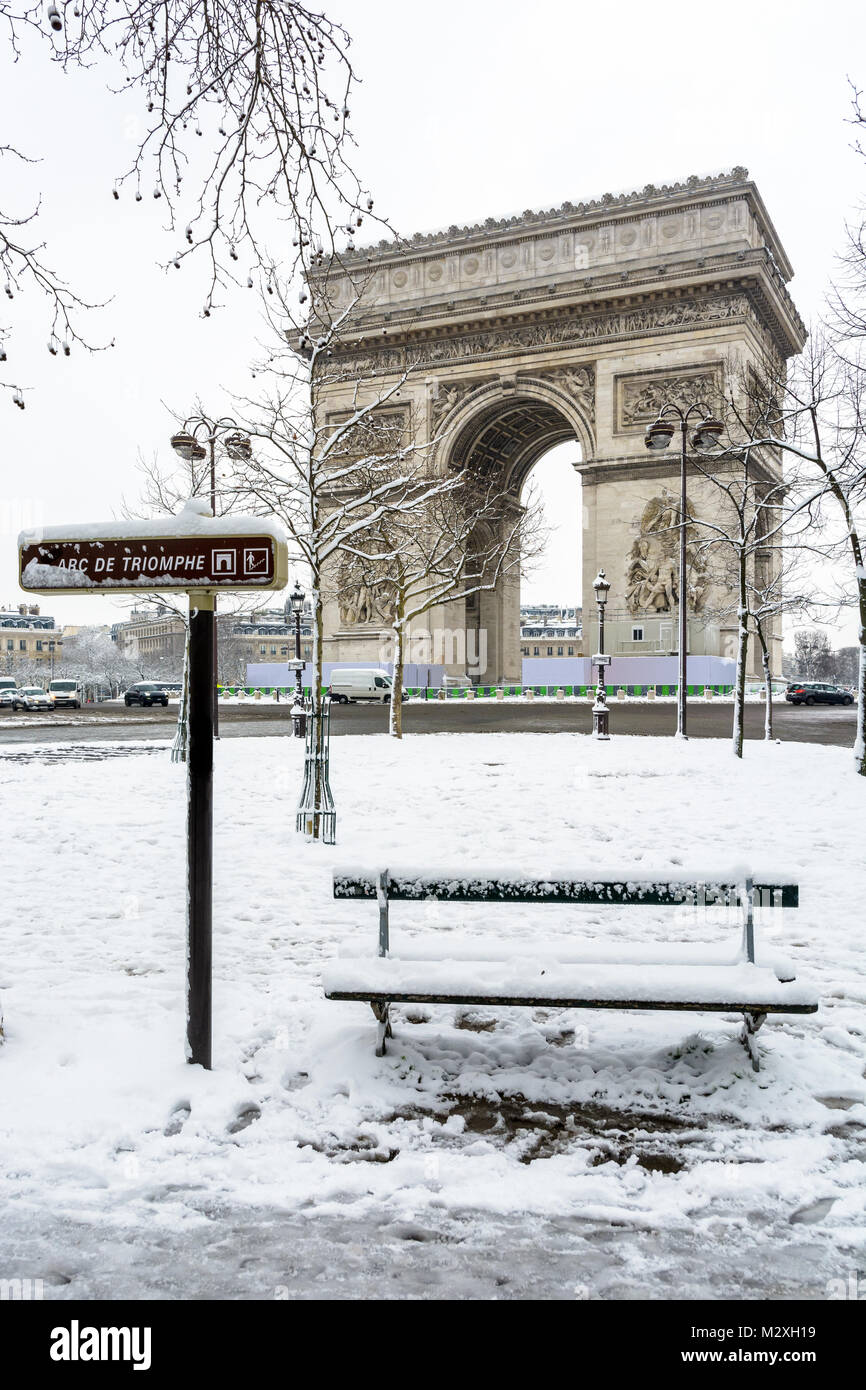 Winter in Paris in the snow. The Arc de Triomphe with a public bench ...