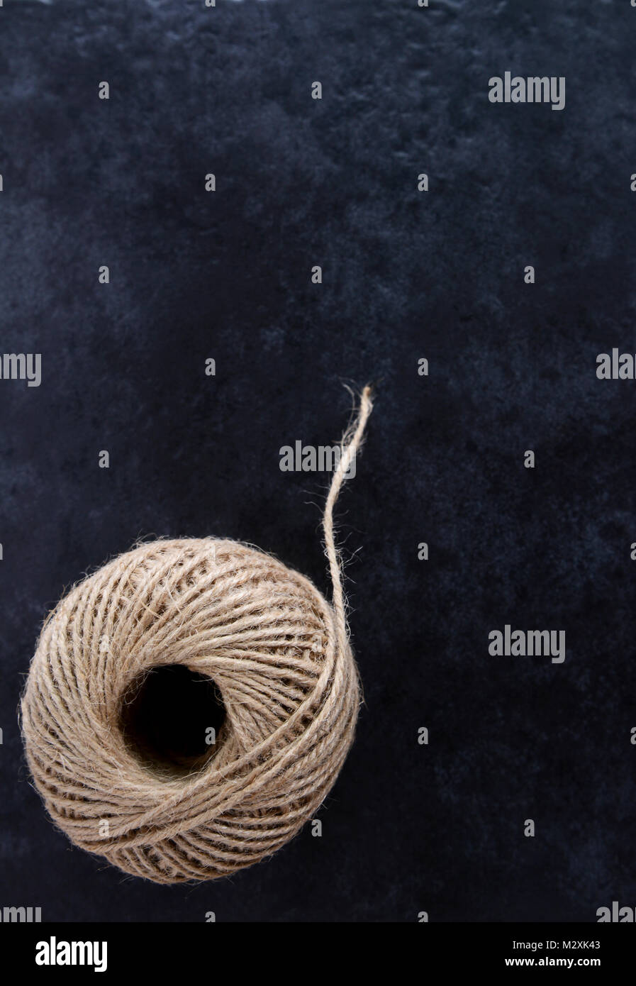 Round ball of hessian twine unfurling on a dark grey background with ...