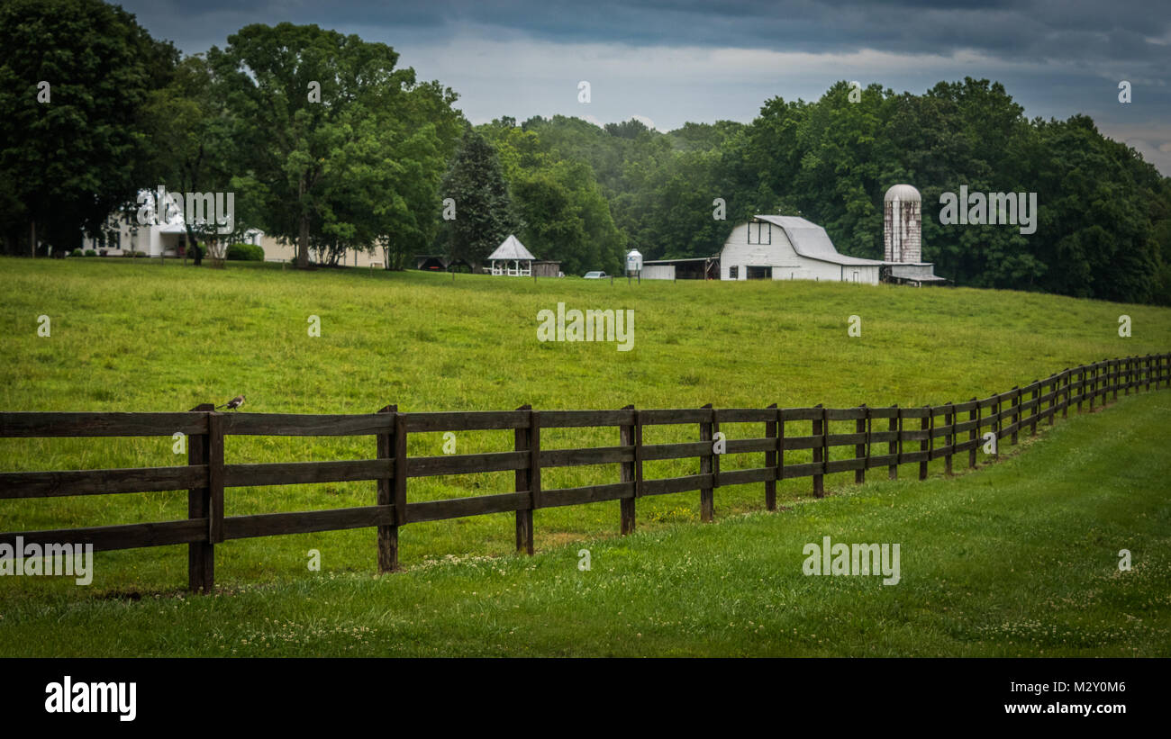 A pasture with a fence and farm, farm house and trees in the background ...