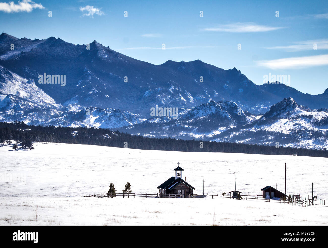 A small log country church nestled in a valley surrounded by tall rocky ...