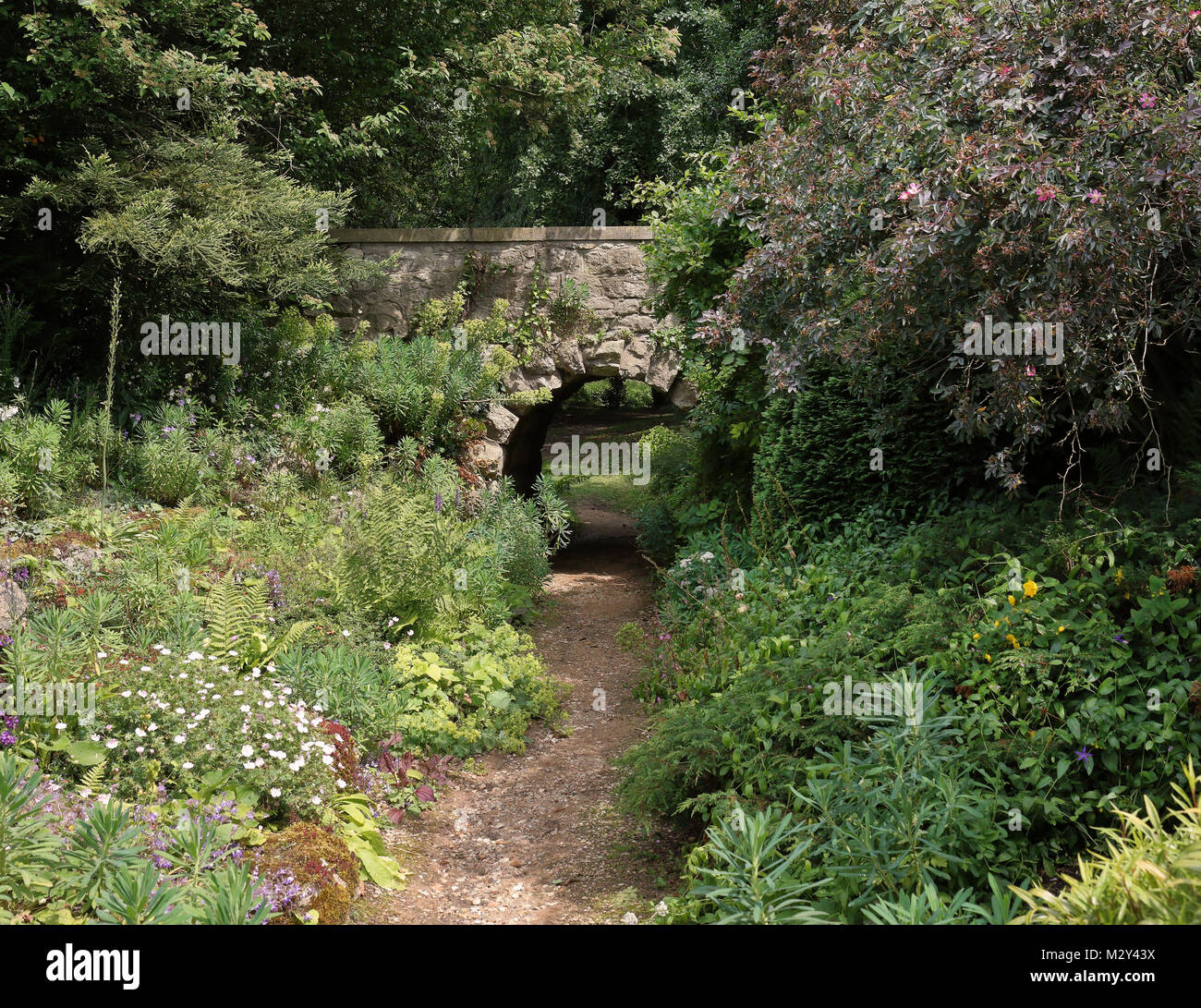 Path between flowerbeds leading to an arched stone bridge Stock Photo ...