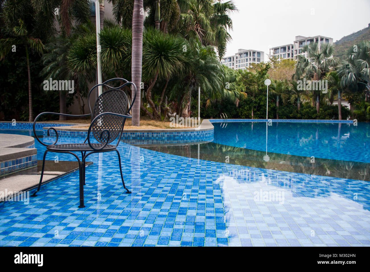 A solitary chair sits alone in a blue swimming pool amid green palm ...