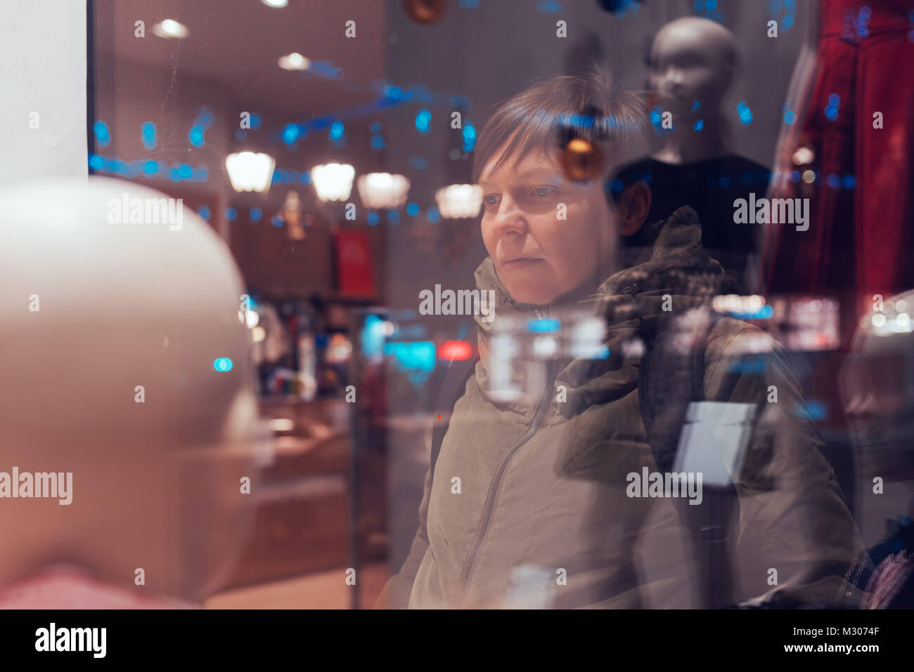 Thoughtful woman looking through shop window at night during the ...