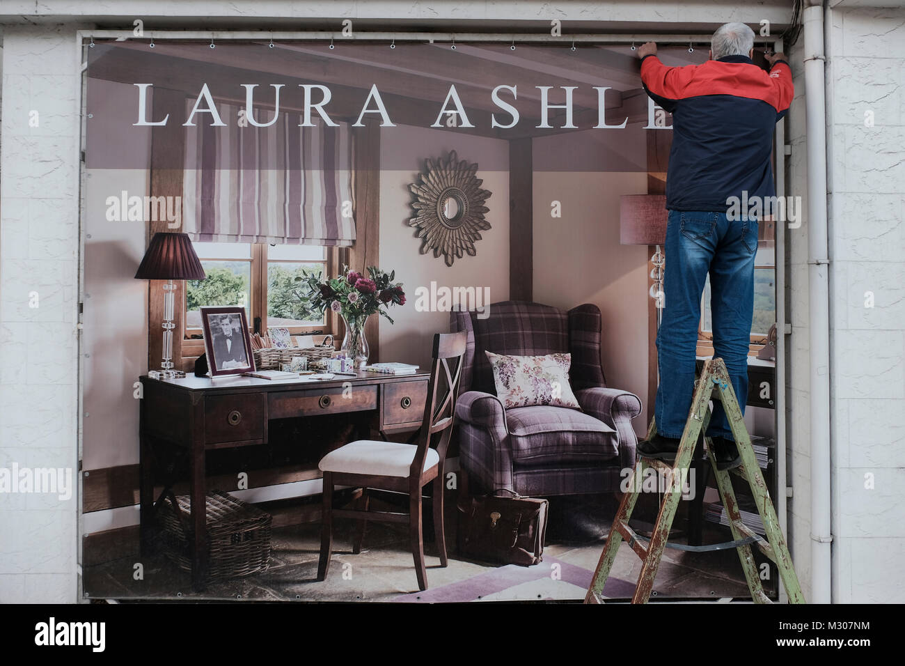 Man hangs an advertisement poster of Laura Ashley a Welsh textile ...