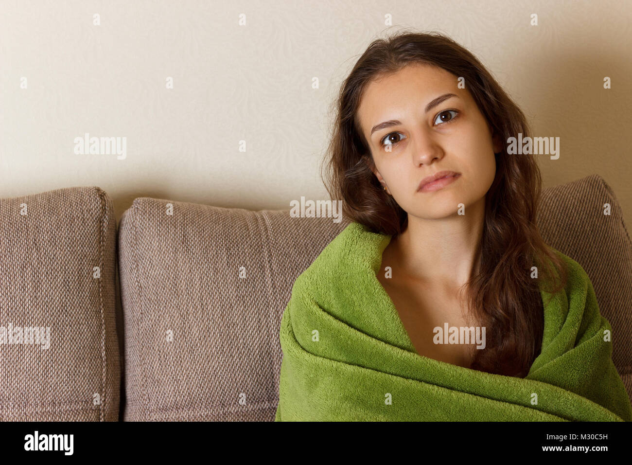 young woman feeling sick or sad wrapped in blanket and sitting on sofa ...