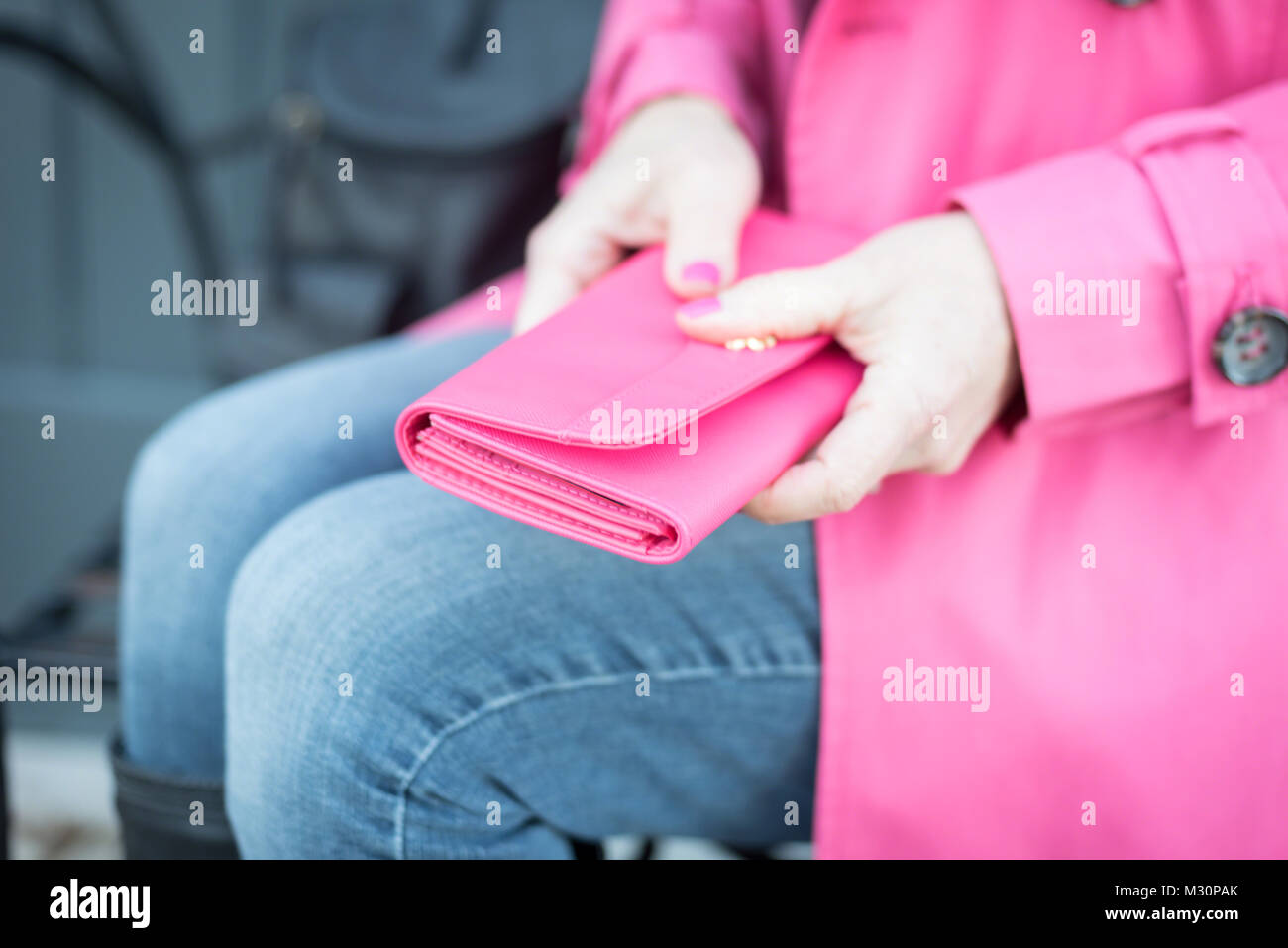 closeup of woman sitting on bench holding pink wallet with pink ...