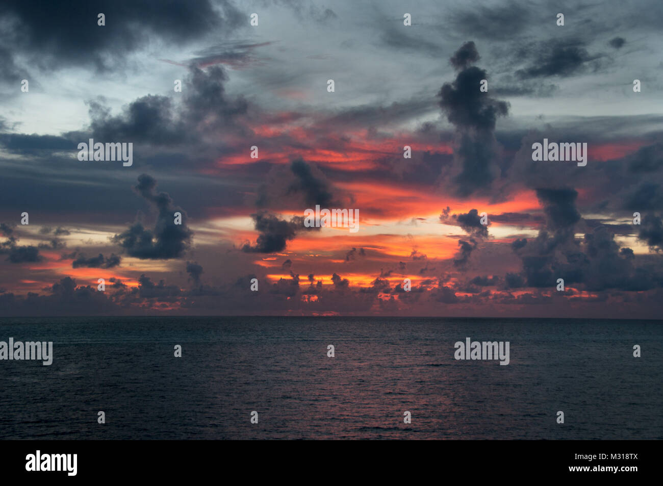 Sunset on the ocean, a bright red glow among the dark gray clouds on ...