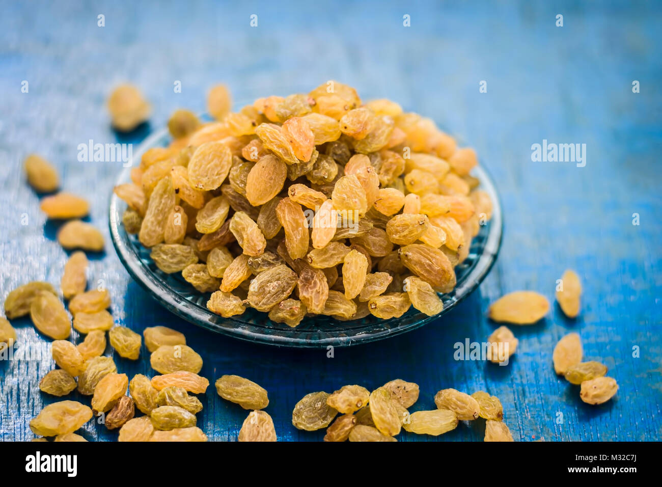 Close up of Golden raisins in a blue glass plate on a wooden surface ...