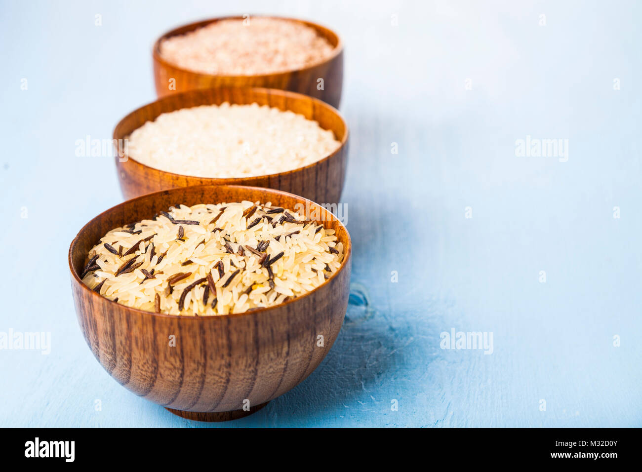 Three bowls with different varieties of rice on a wooden background ...