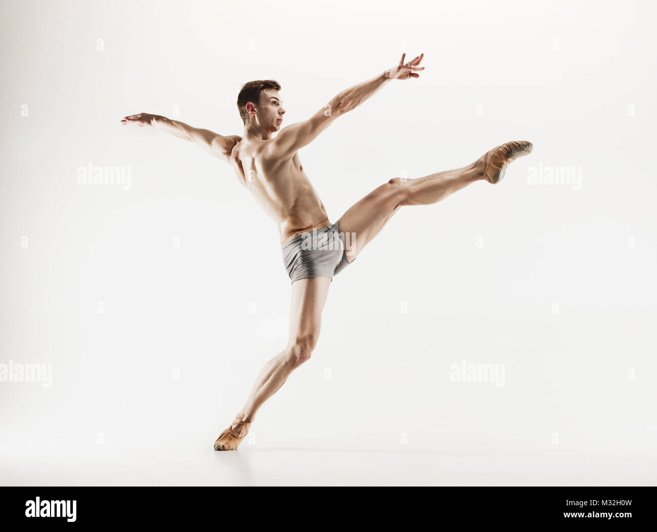 Athletic ballet dancer in a perfect shape performing over the grey ...