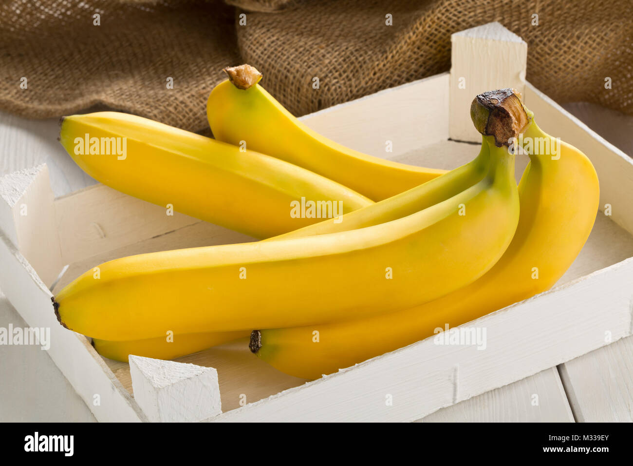 Bundle of fresh, yellow, ripe bananas in white wooden box on wood table ...