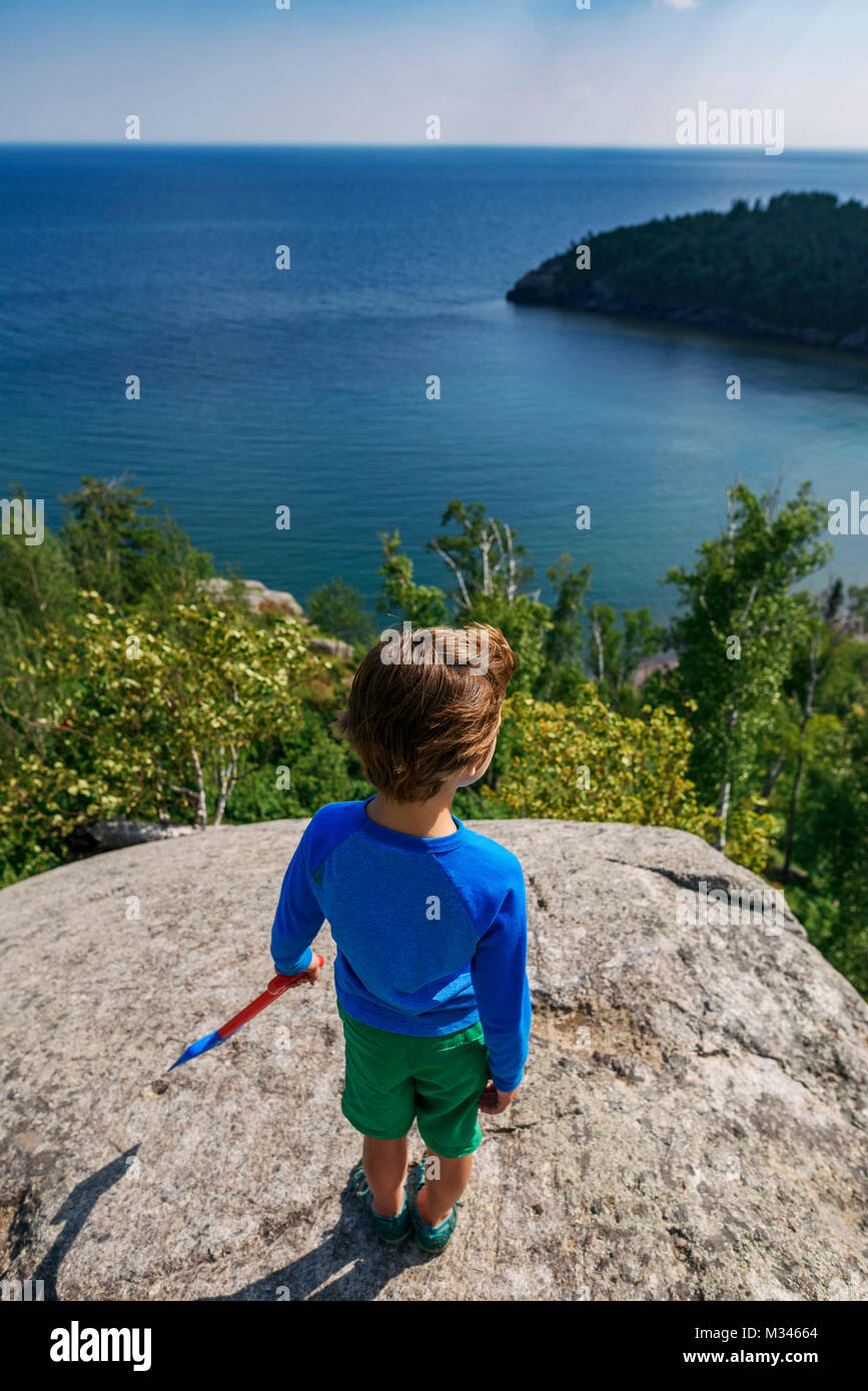 Boy standing on cliff looking at ocean Stock Photo - Alamy