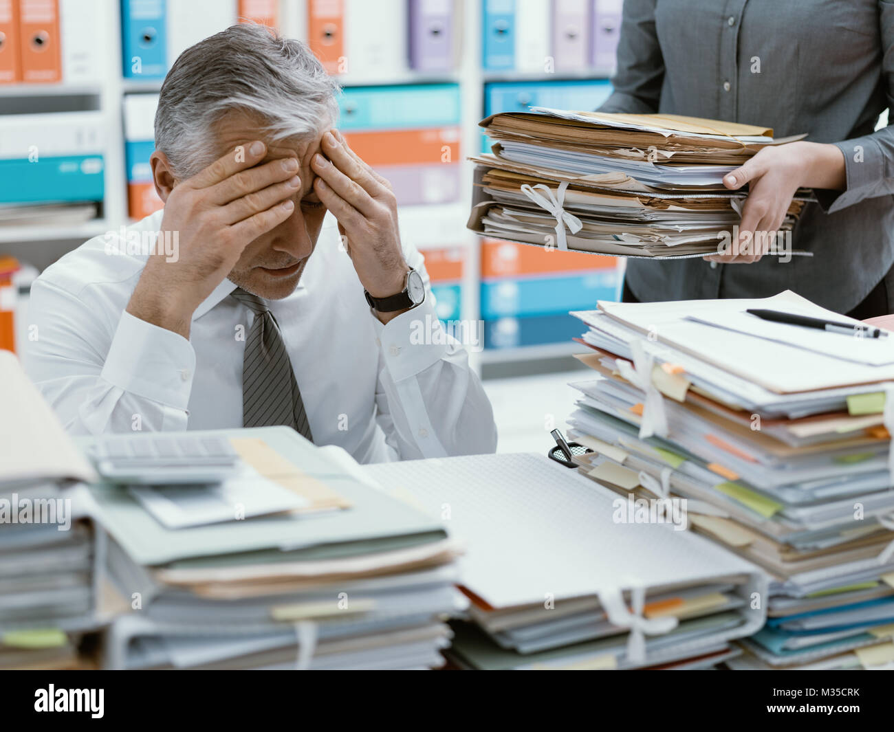 Stressed businessman working at office desk and overloaded with work ...