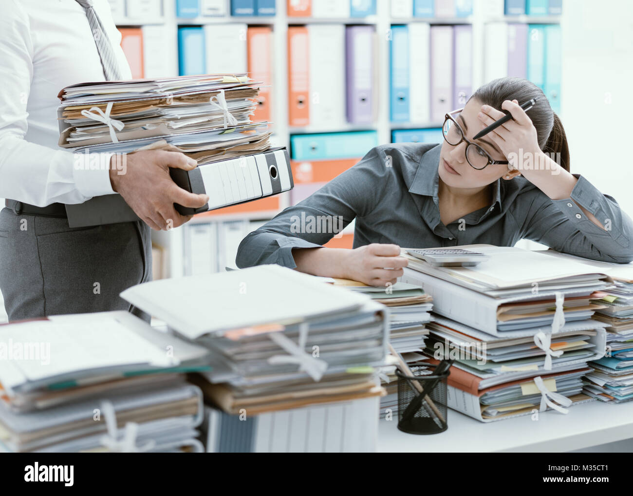 Young stressed secretary in the office overwhelmed by work and desk ...