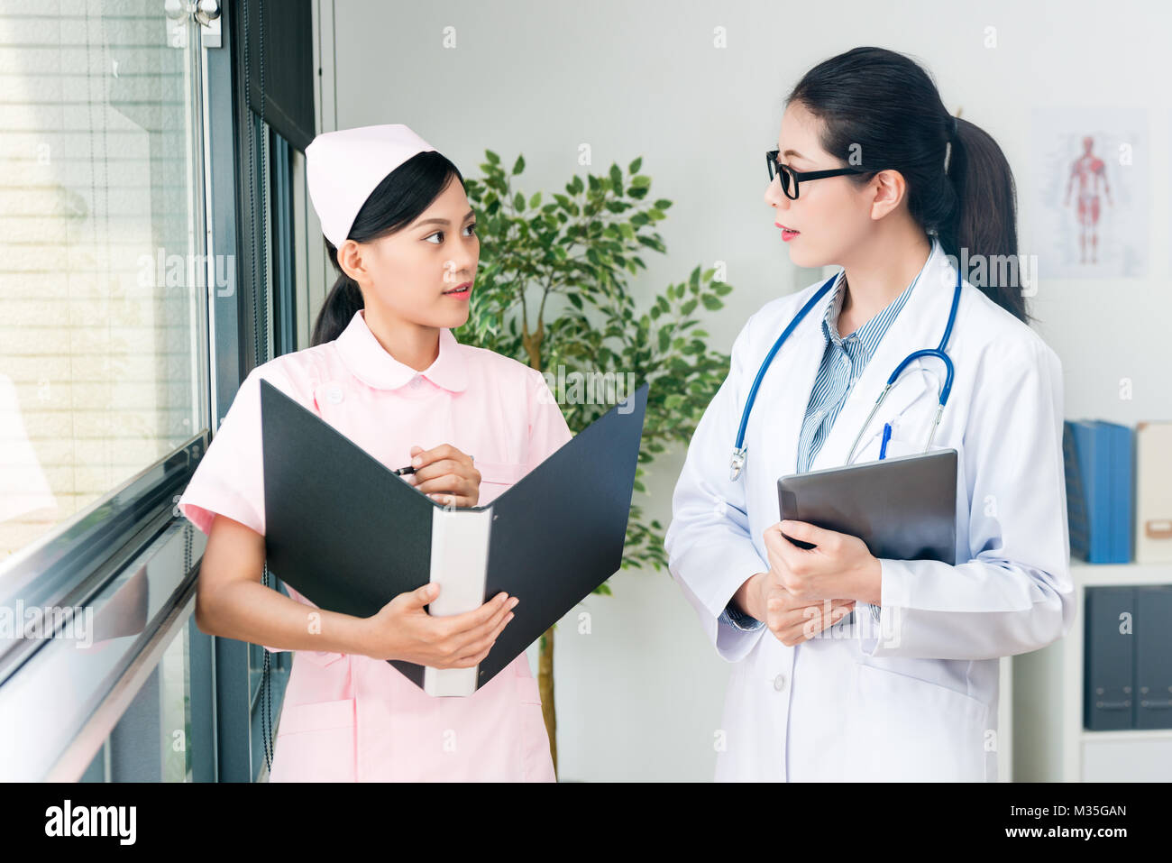 smiling young nurse holding work file talking with doctor and ...