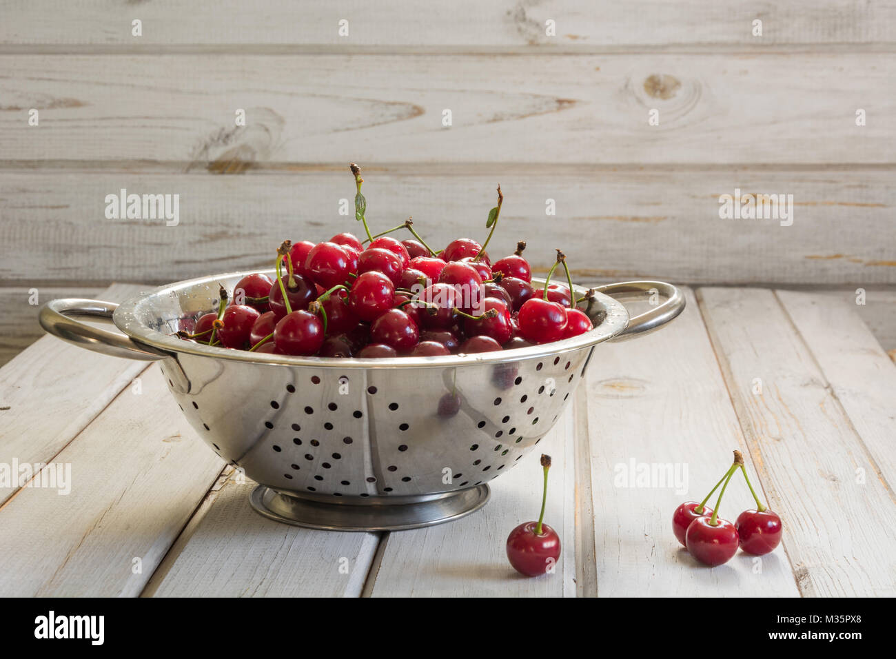 Metal colander full of freshly cherries over a rustic board. Cherry ...