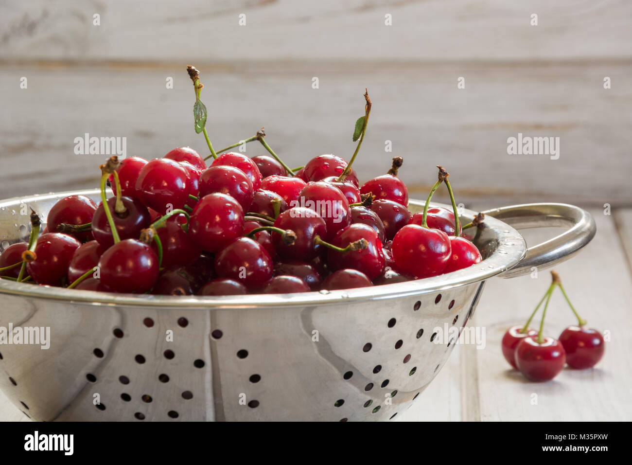Metal colander full of freshly cherries over a rustic board. Cherry ...