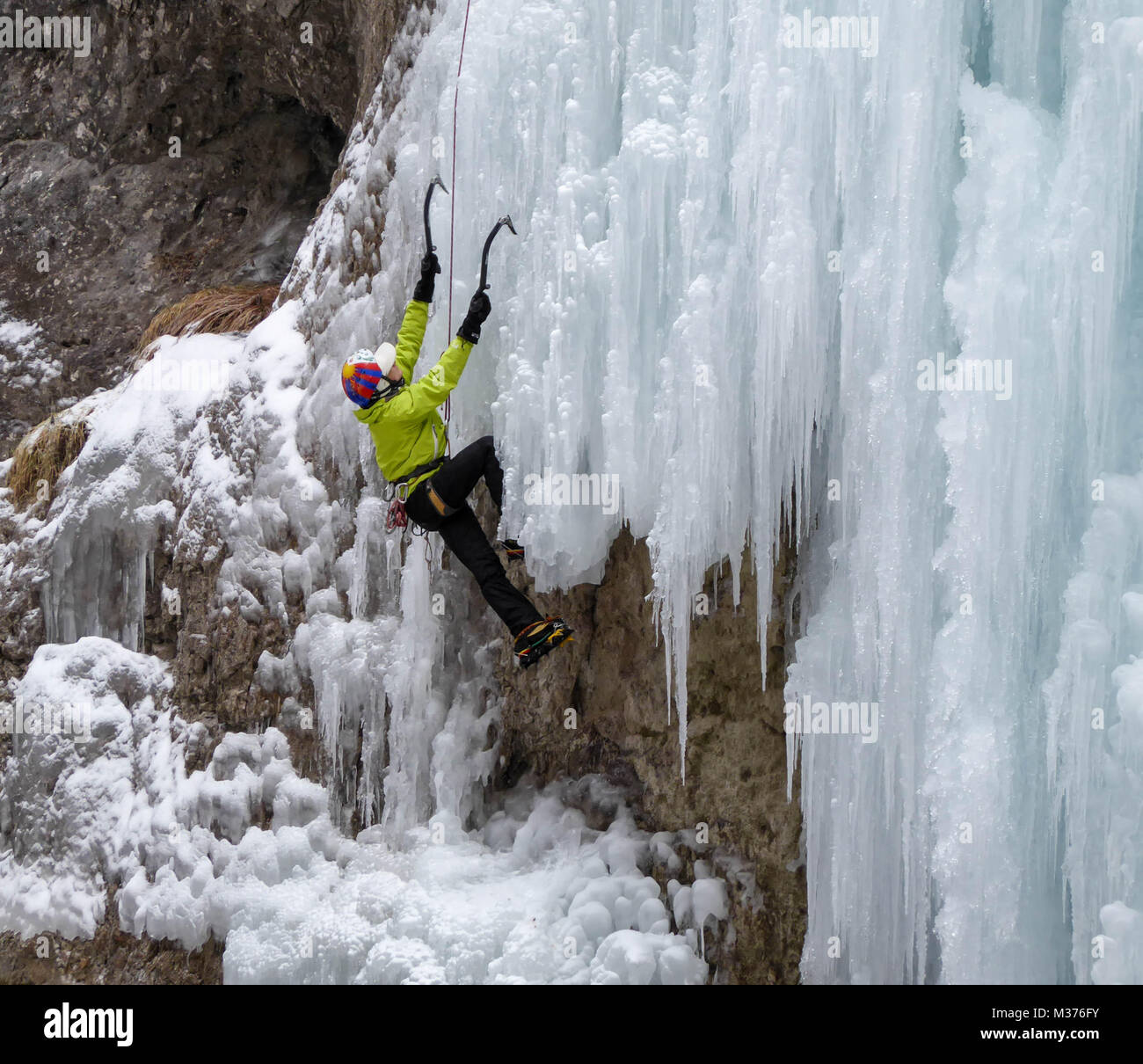male ice climber in a yellow jacket on a steep frozen waterfall ice ...