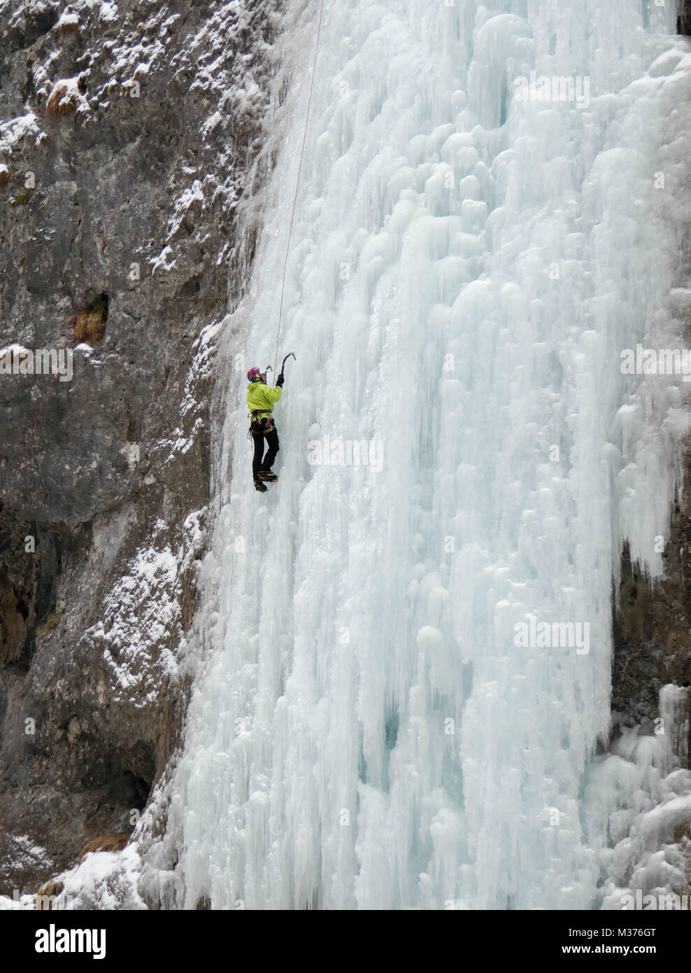 male ice climber in a yellow jacket on a steep frozen waterfall ice ...