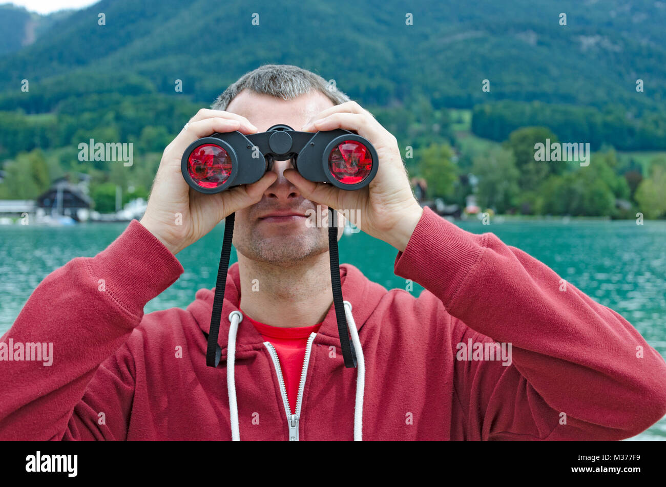 A middle-aged man with binoculars observing nature at the lake on a ...
