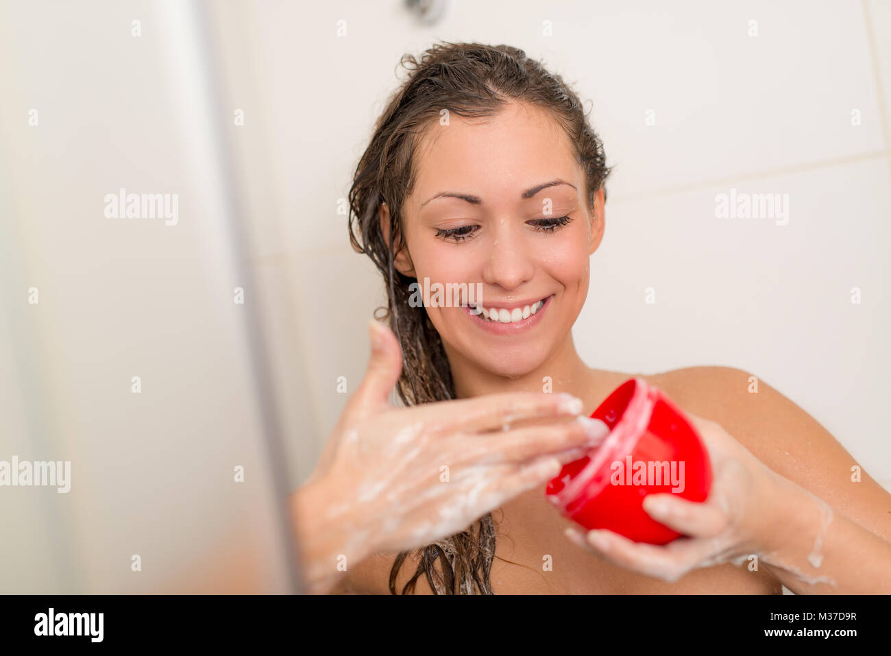 Beautiful smiling young woman washing her long hair. She is holding ...