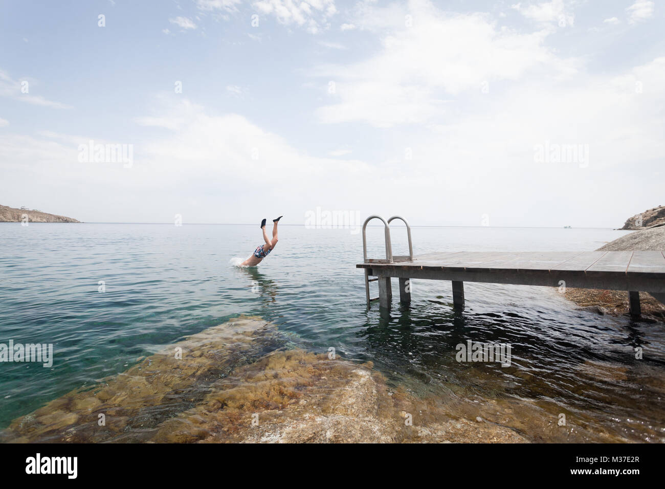 Vacation view with a man jumping in sea from a bridge Stock Photo - Alamy