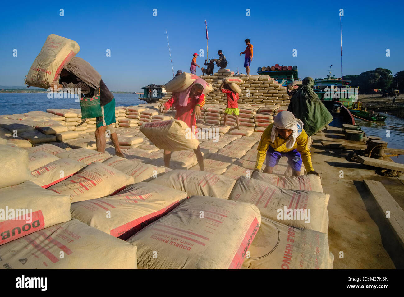 Workers are loading cement bags on a boat in the harbour at the ...